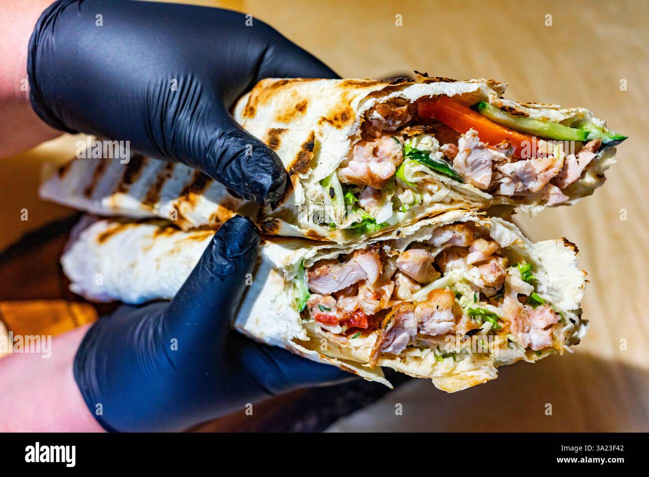 A chef in black gloves presents a freshly prepared grilled chicken wrap ...