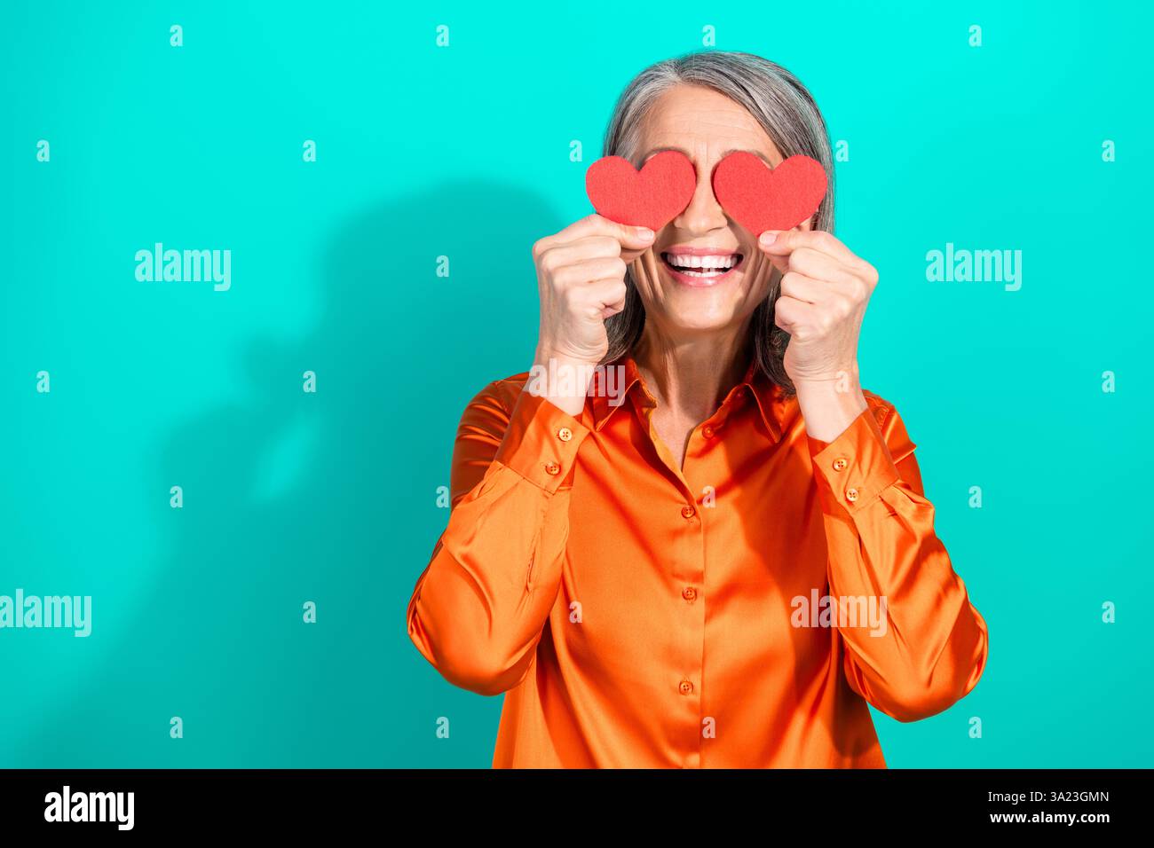 Joyful elderly woman covering eyes with heart shapes, expressing ...