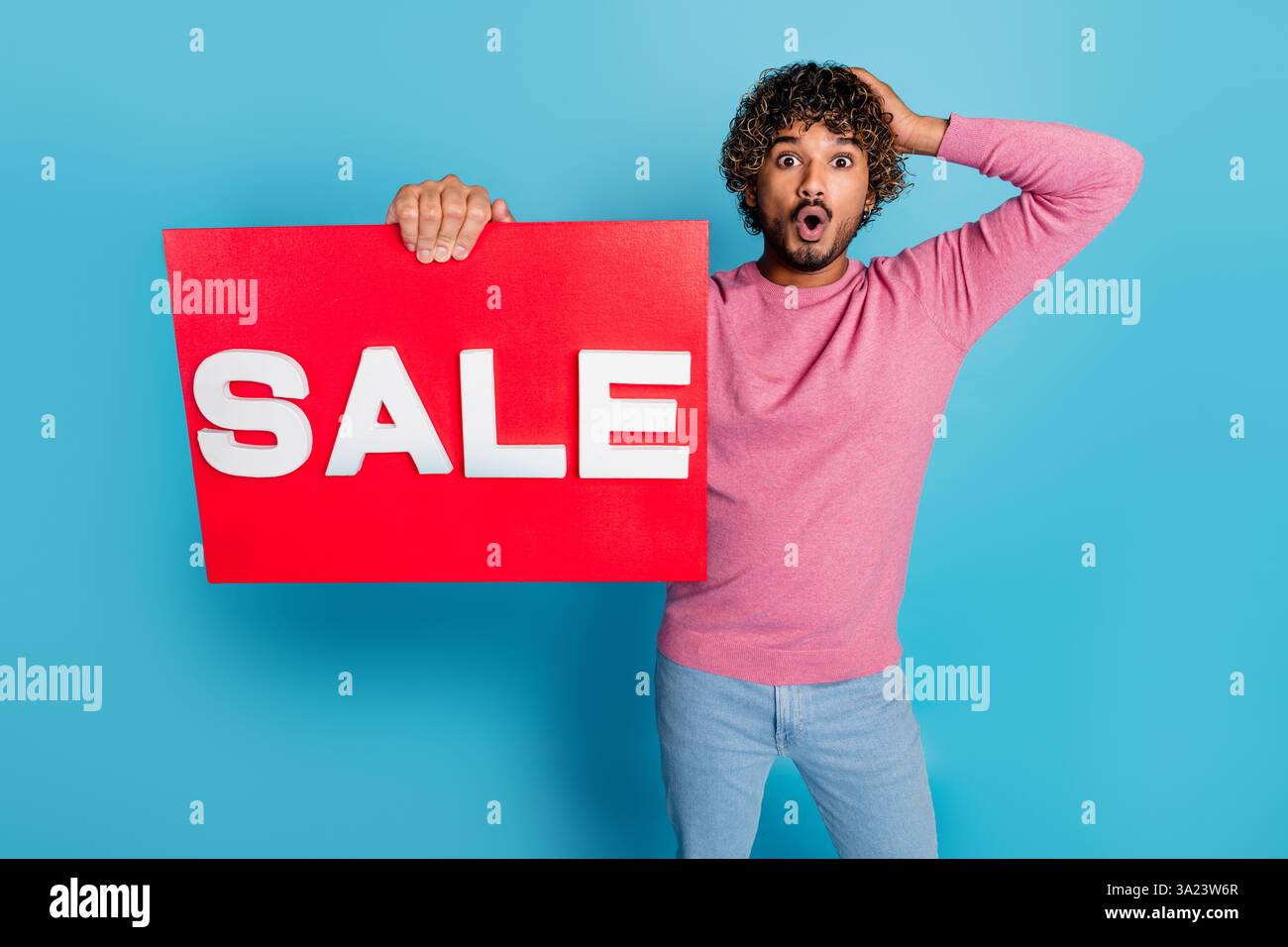 Excited young man holding a bold red sale sign against a bright blue ...