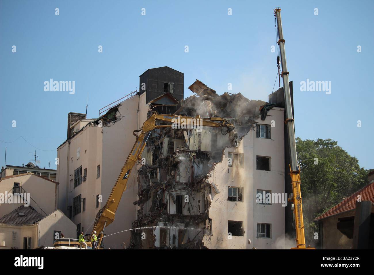 Construction workers operate heavy machinery to demolish a multi-story building in an urban ...