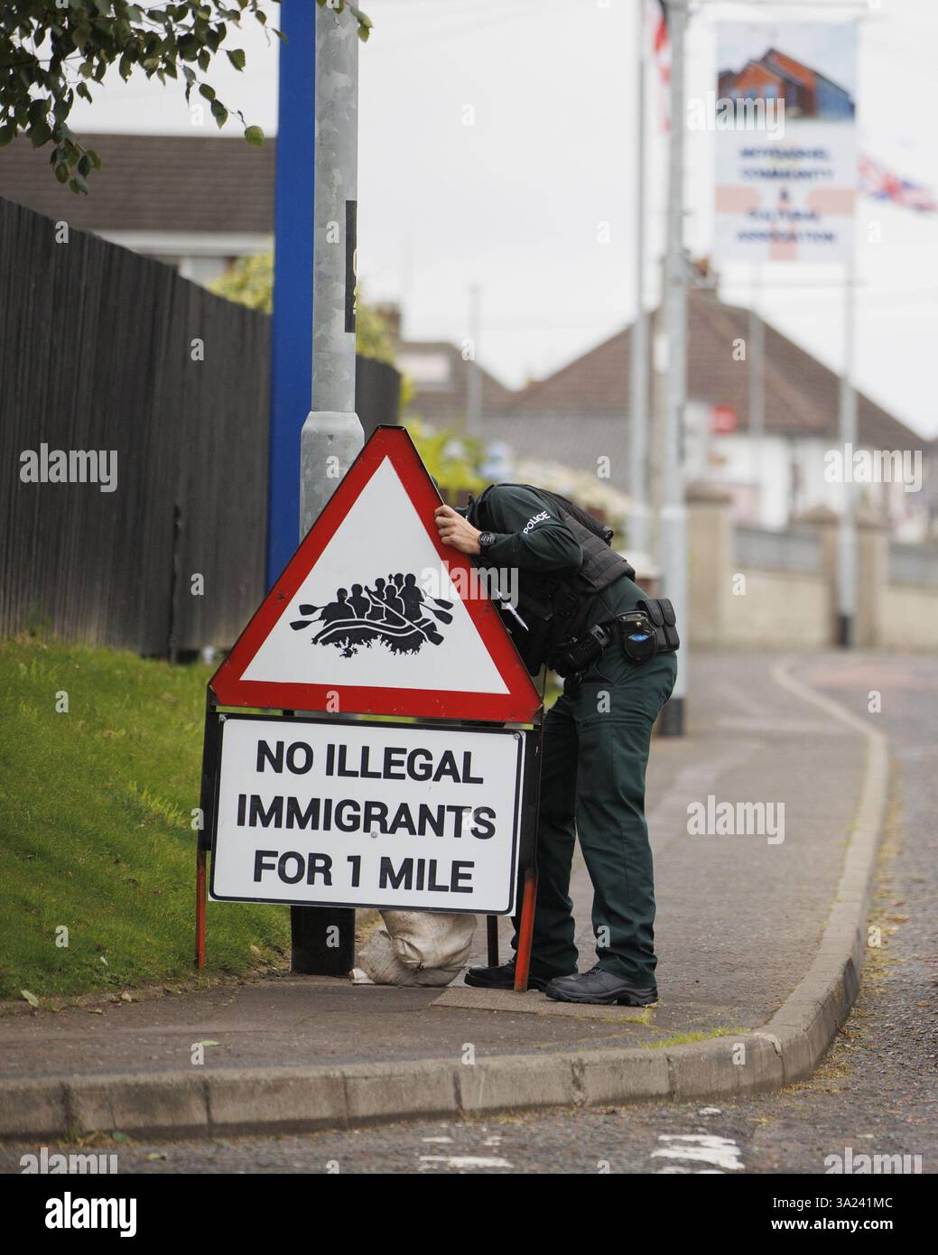 PSNI officer removing a road sign with image of people a dingy boat ...