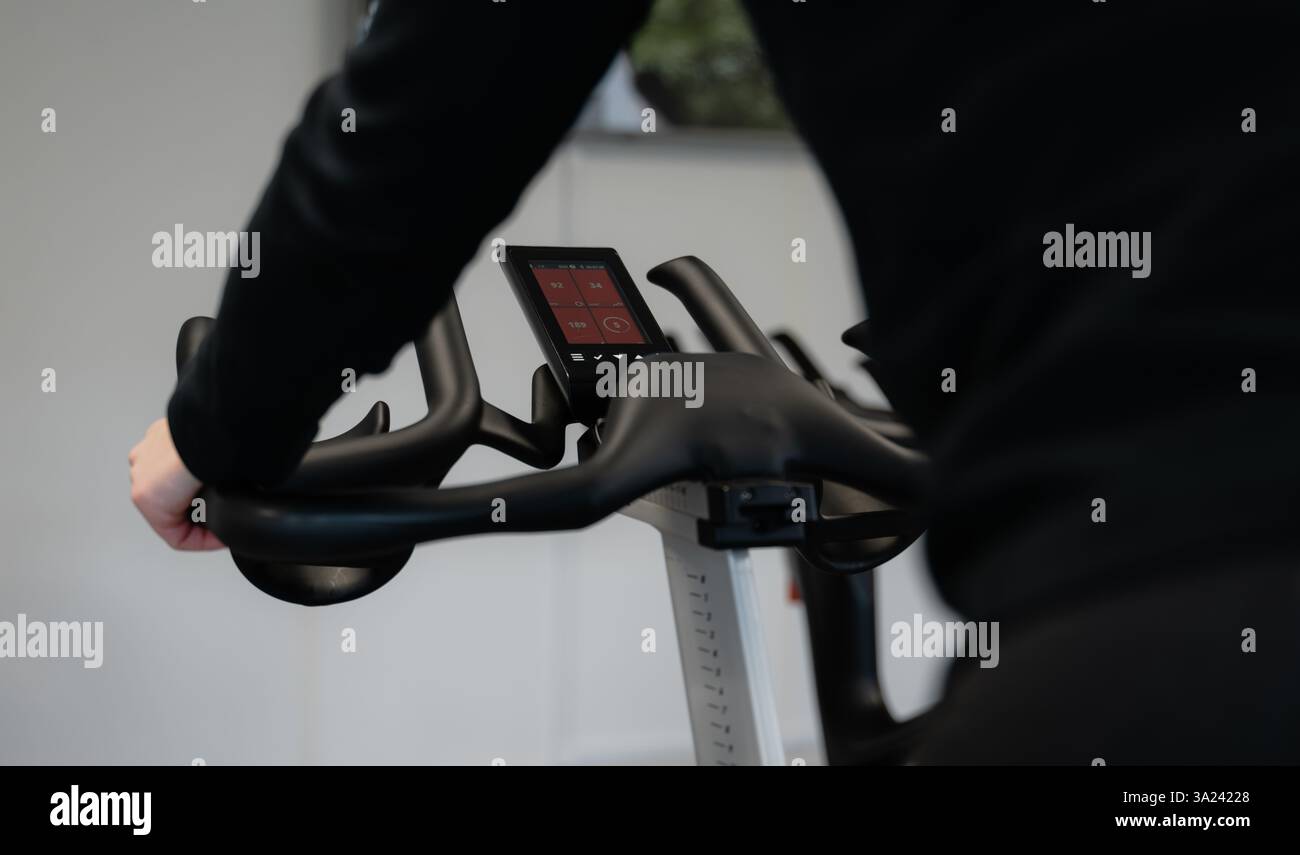 A person is riding a spin bike with a digital screen showing the time ...