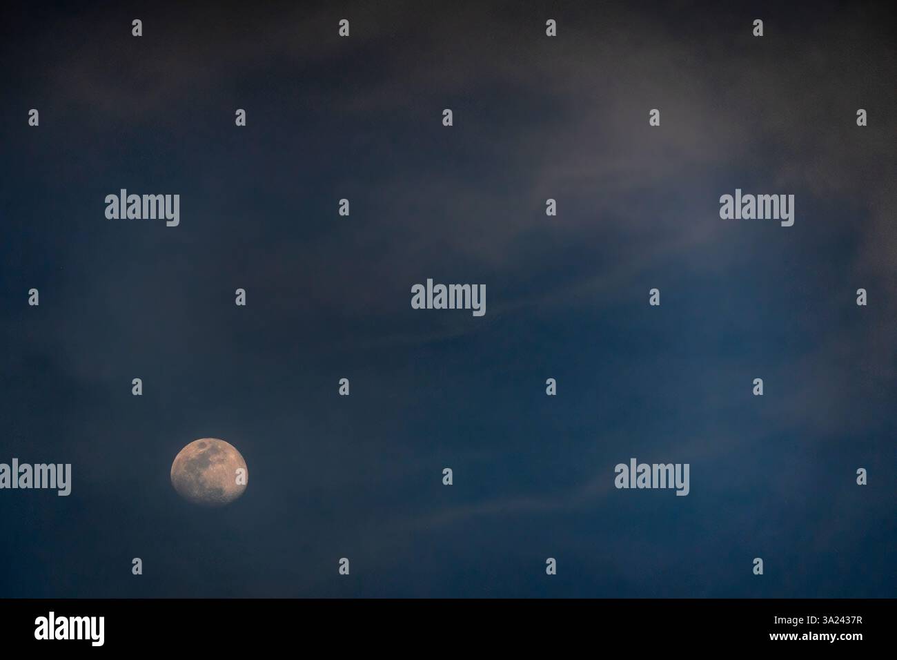 Three quarter moon phase appearance with light clouds and dark blue sky ...