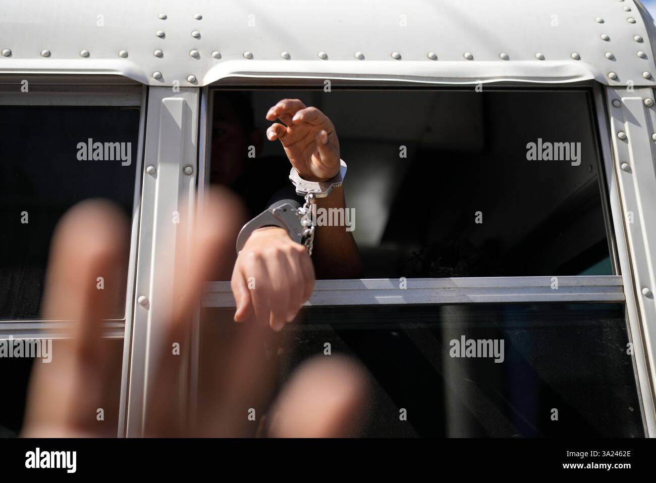 Migrants from Colombia rest their handcuffed hands out the window of a ...