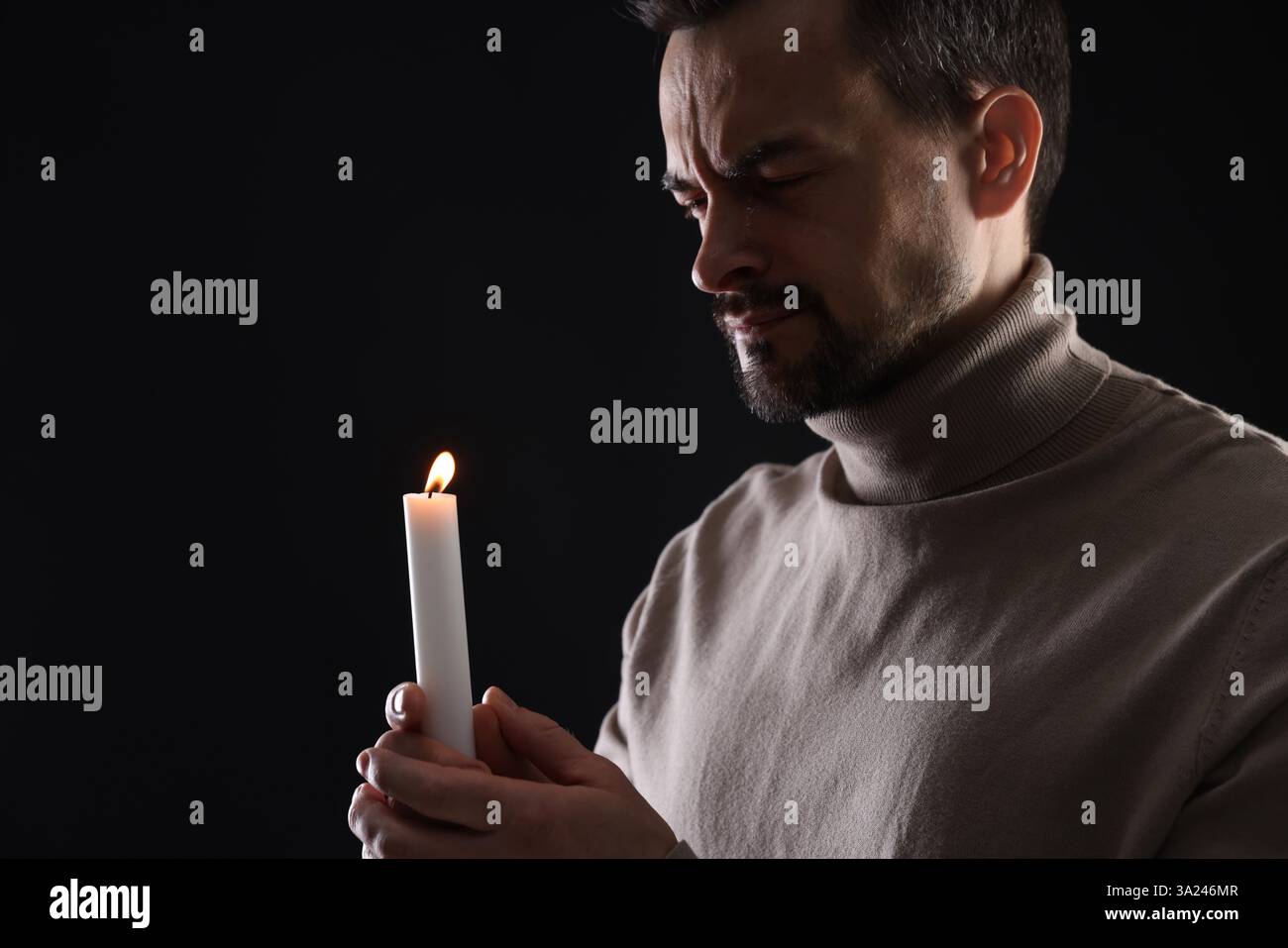Sad man with burning candle crying on black background, space for text ...