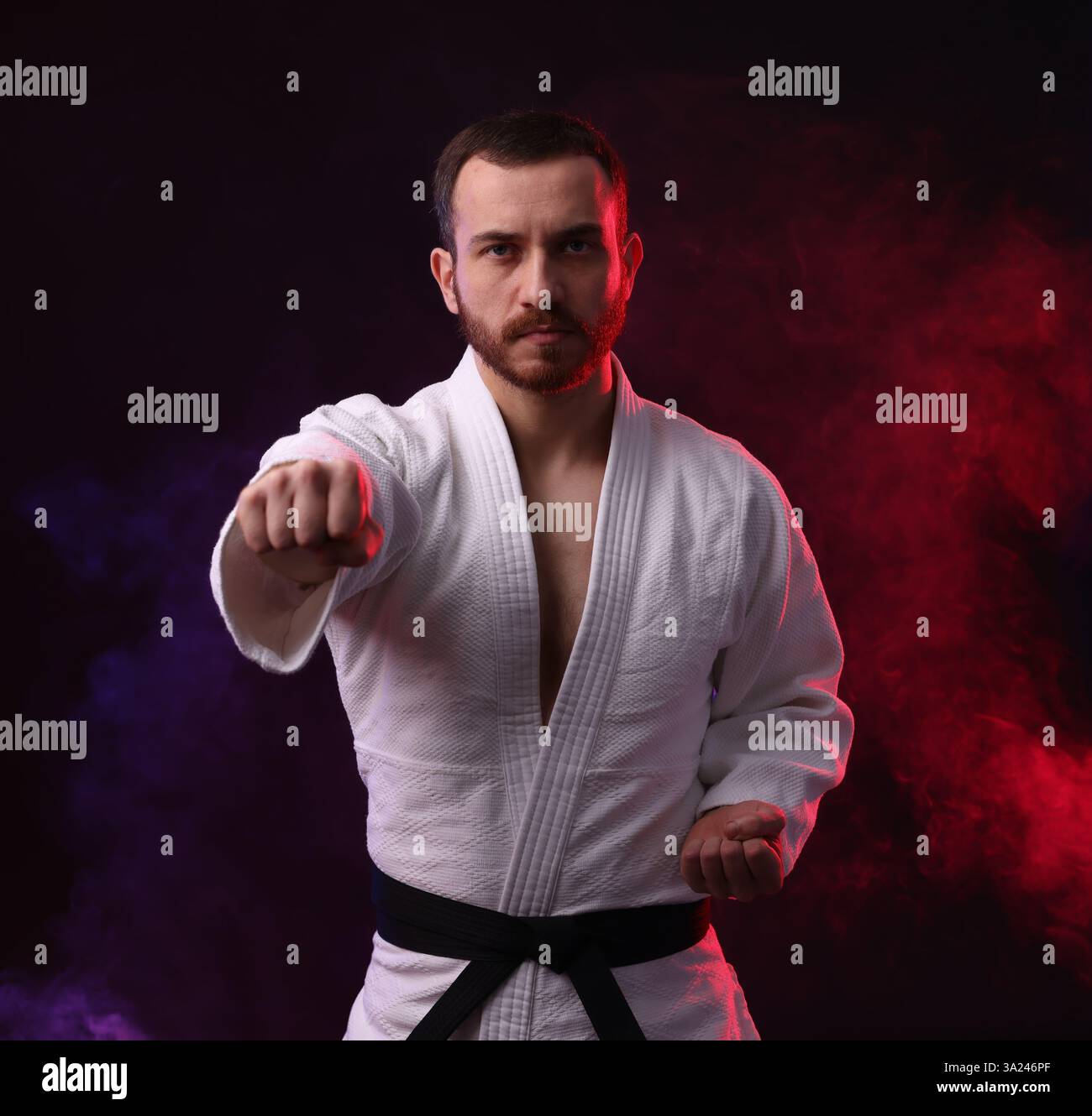 Man wearing uniform practicing karate in color lights and smoke against ...