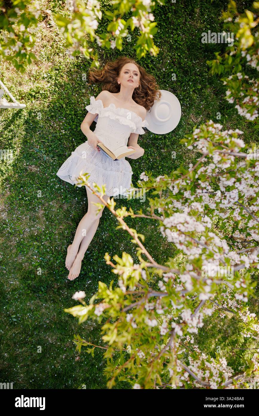 Romantic woman in a white dress lying on green grass under cherry ...