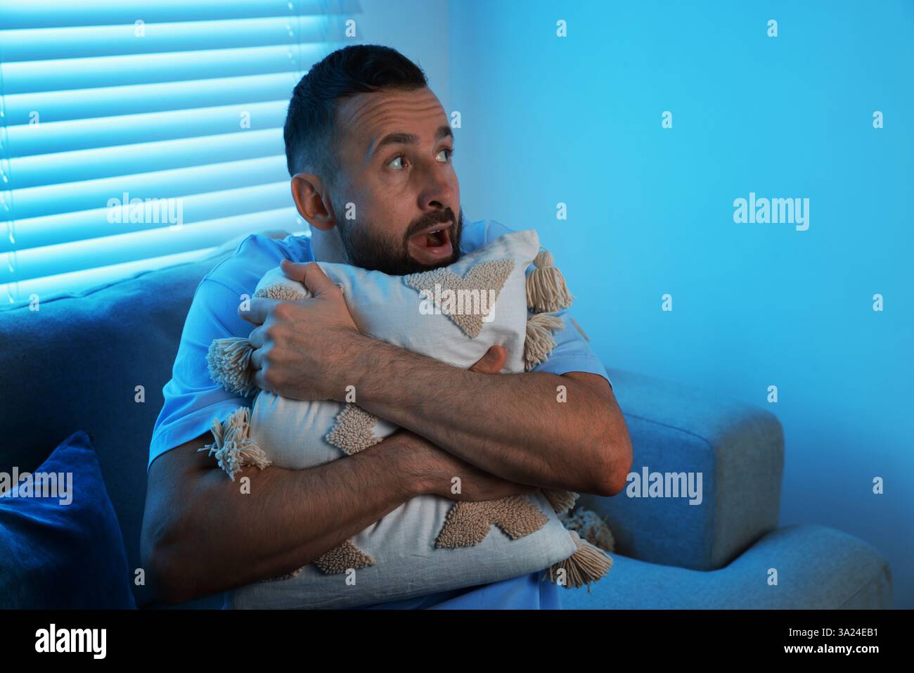 Fear of darkness. Scared man hugging pillow on couch in dark room ...