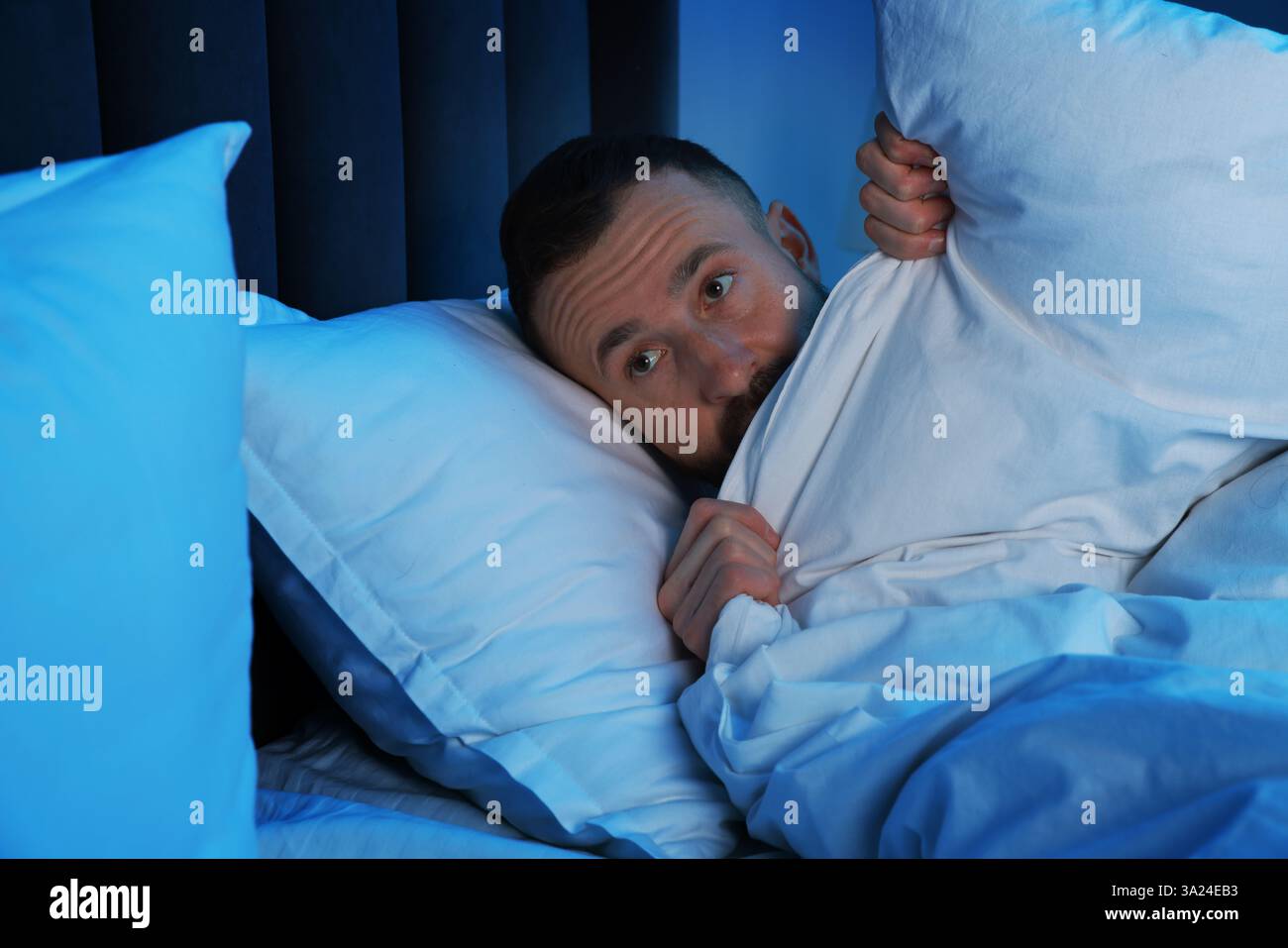Fear of darkness. Scared man lying on bed in room at night Stock Photo ...