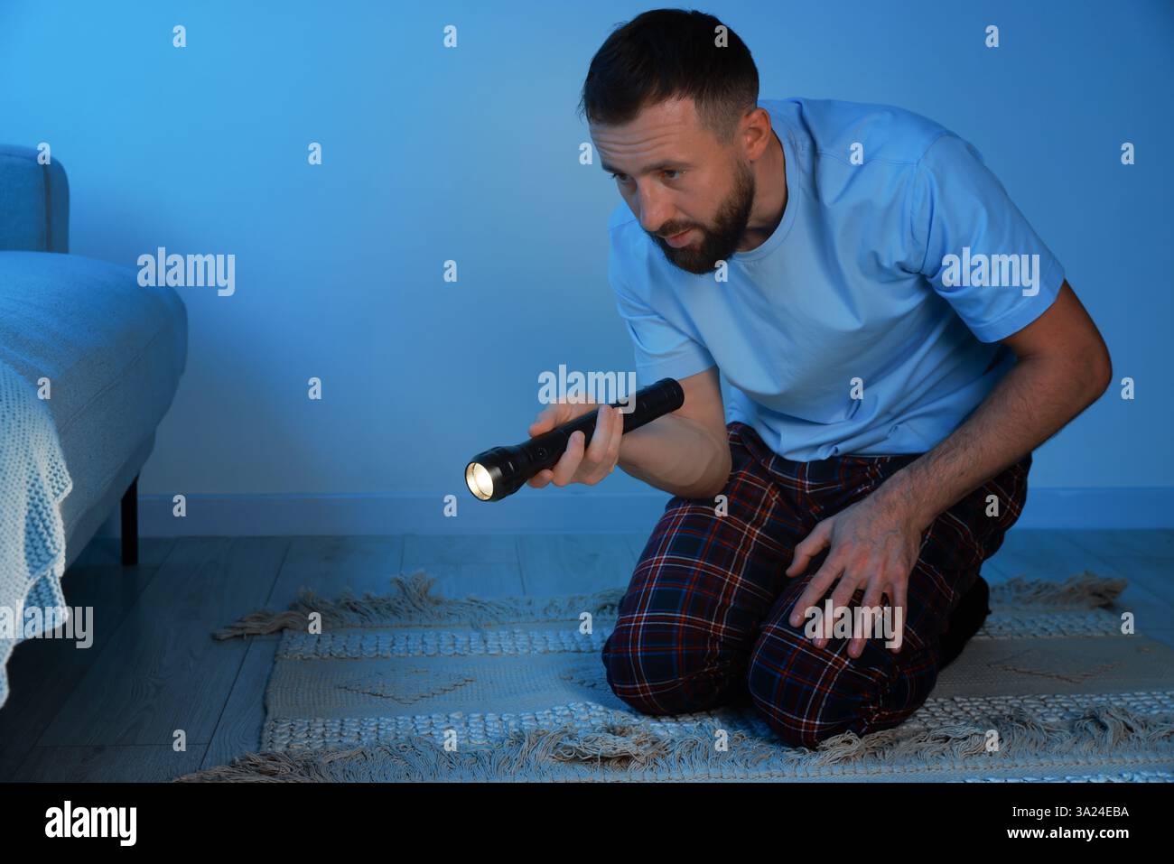 Fear of darkness. Scared man looking under bed with flashlight indoors ...