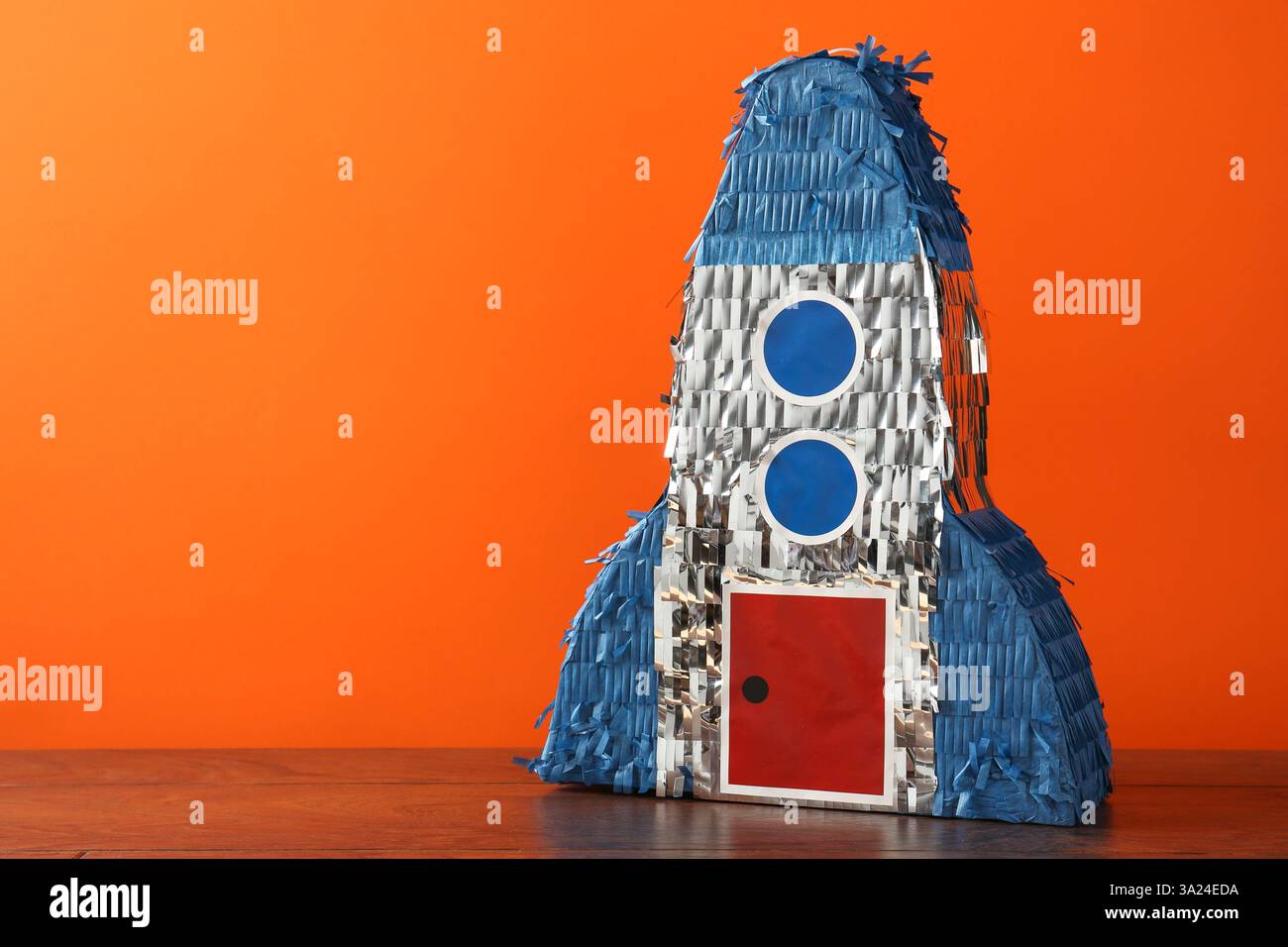 Bright pinata in shape of spaceship on table against orange background ...