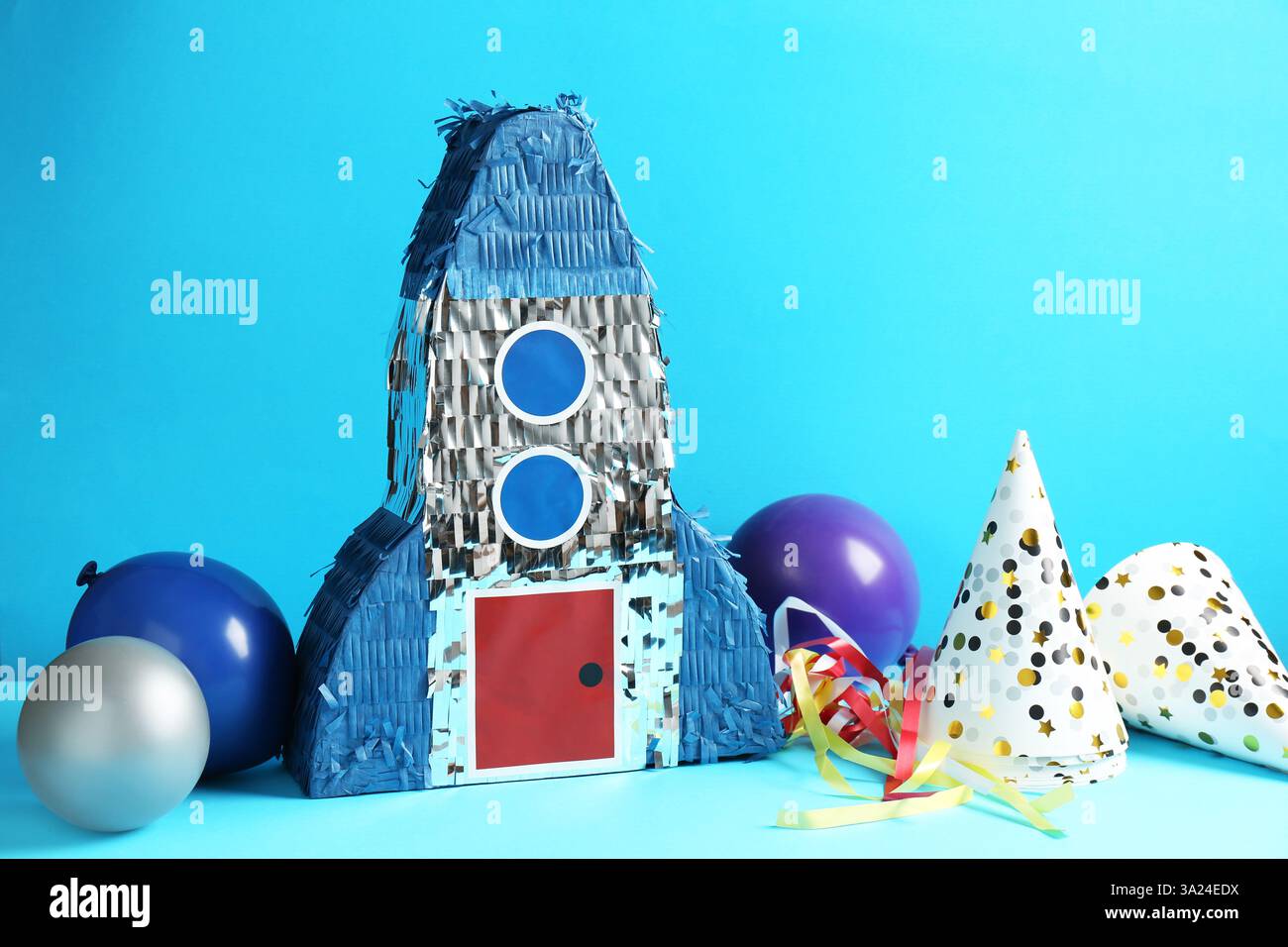 Beautiful pinata in shape of rocket, party cones and balloons on blue ...