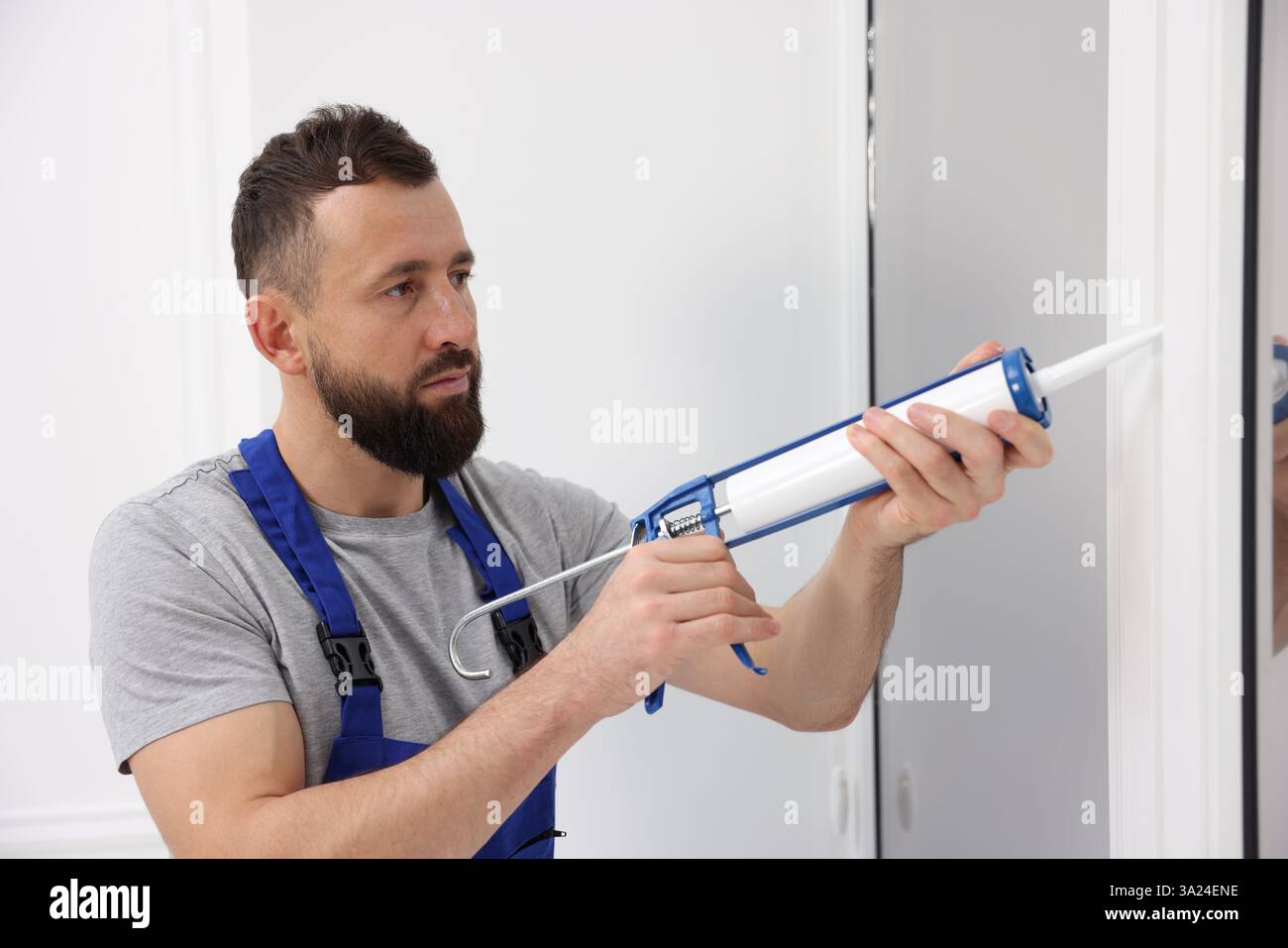 Worker with caulking gun sealing window indoors Stock Photo - Alamy