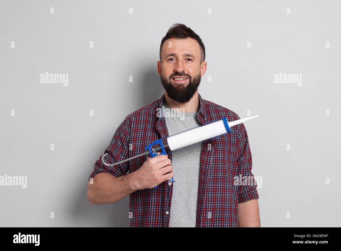Man with caulking gun on gray background Stock Photo - Alamy