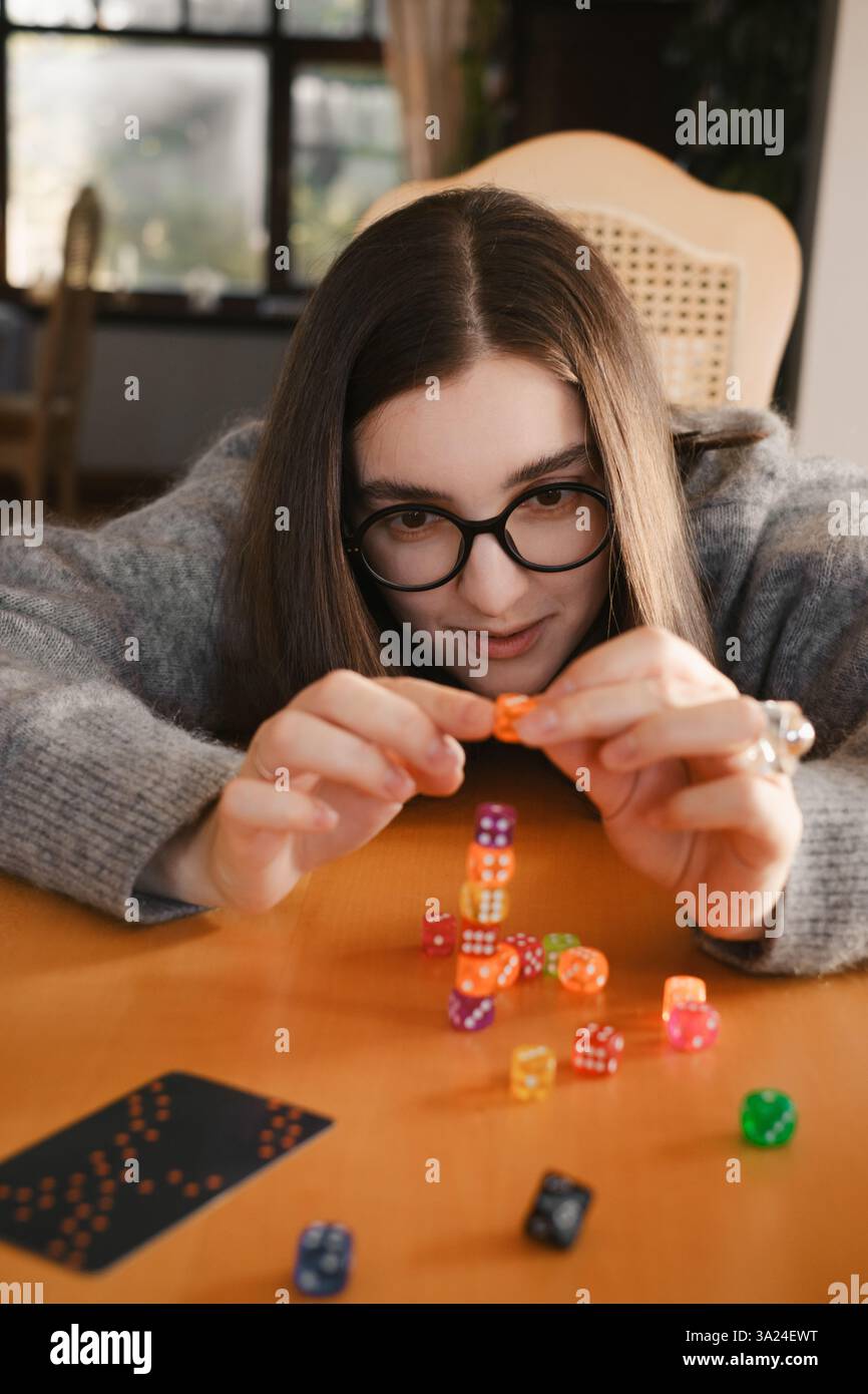 Young woman focuses intently while stacking colorful dice on wooden ...