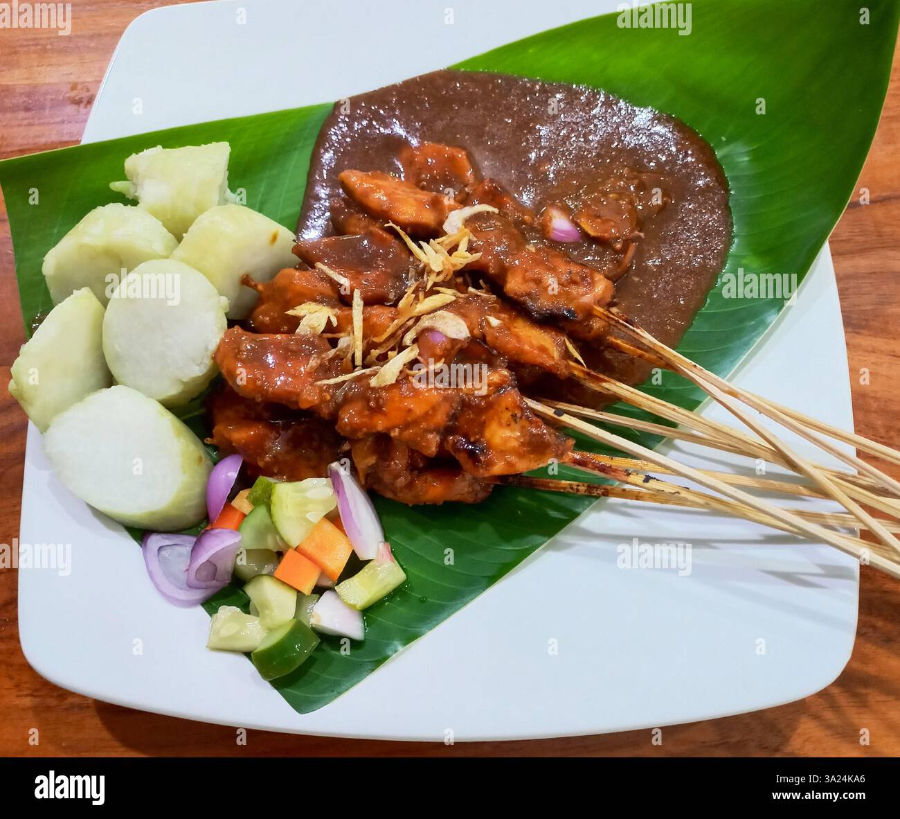Indonesian Sate Ayam with lontong rice cake served on a banana leaf for ...