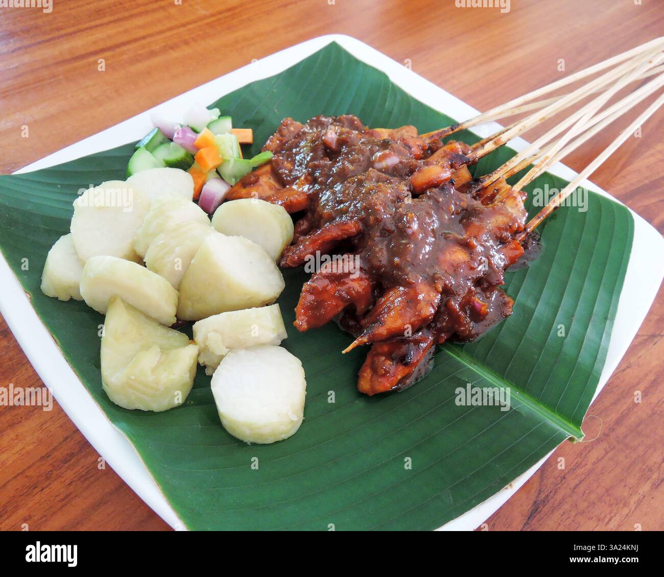 Indonesian Sate Ayam with lontong rice cake served on a banana leaf for ...