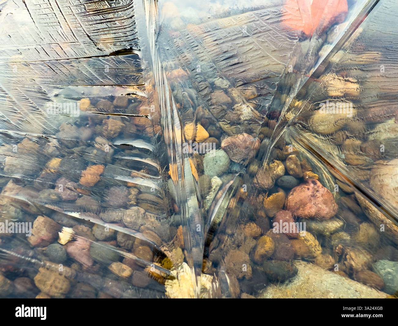 Pattern in ice of frozen water above layer of pebbles in multiple ...