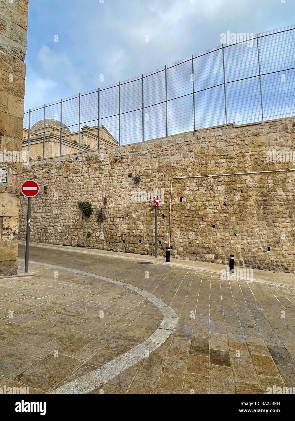 A quiet street in Jerusalem’s Old City, lined with ancient stone walls and modern barriers Stock ...