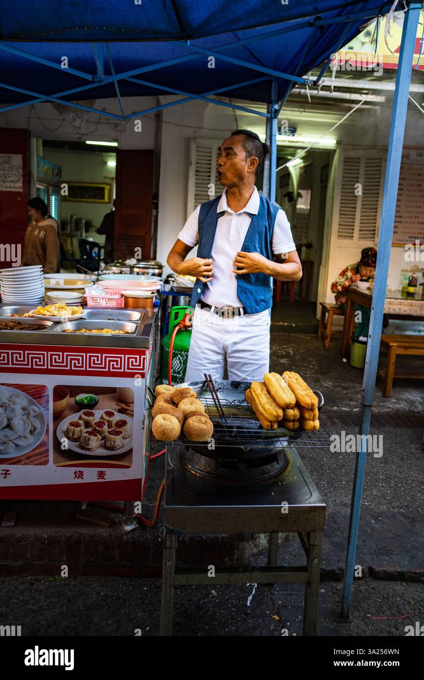Street food vendor preparing traditional snacks under a blue canopy ...