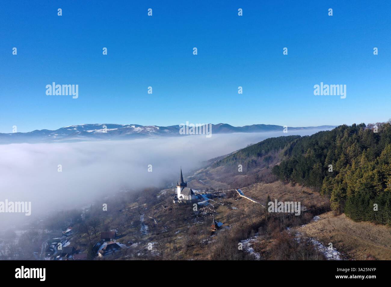 Aerial view of foggy misty mountain village and church tower at winter ...
