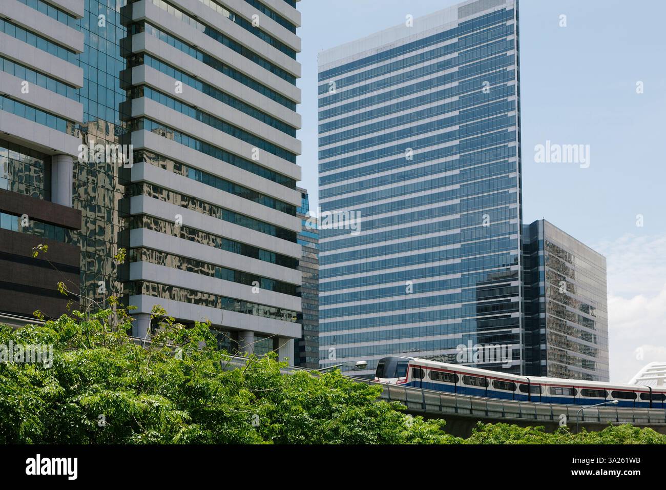 A mass transit train on an elevated track passes modern glass buildings ...