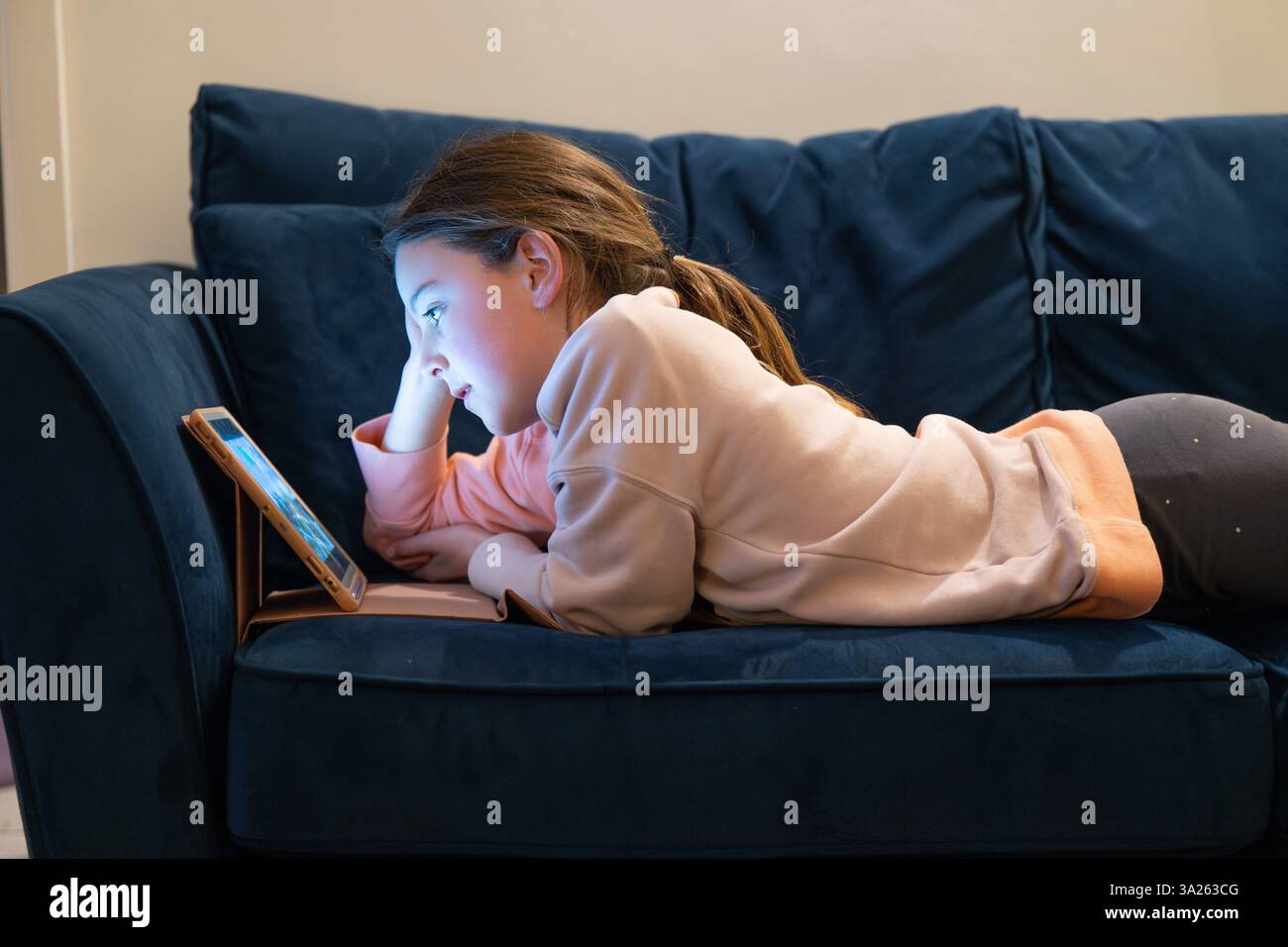 Girl relaxing on sofa with face lit up by screen of tablet Stock Photo ...