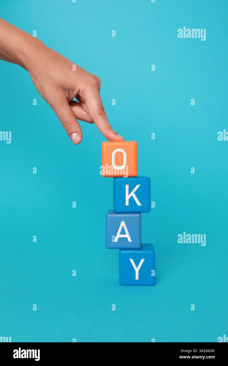 Woman making word Okay with colorful cubes on light blue background ...