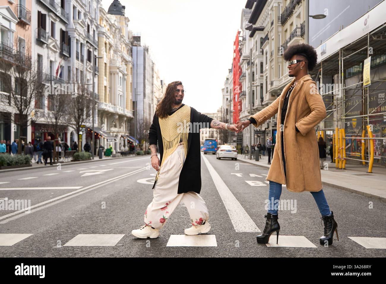 Two androgynous people holding hands crossing a street in a big city ...