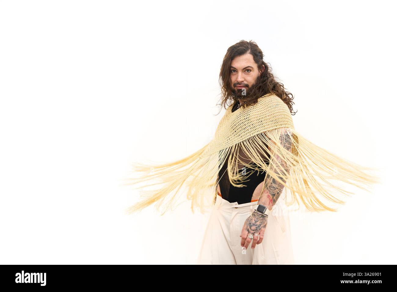 Latin transgender model with beard and long hair wearing fringe shawl ...