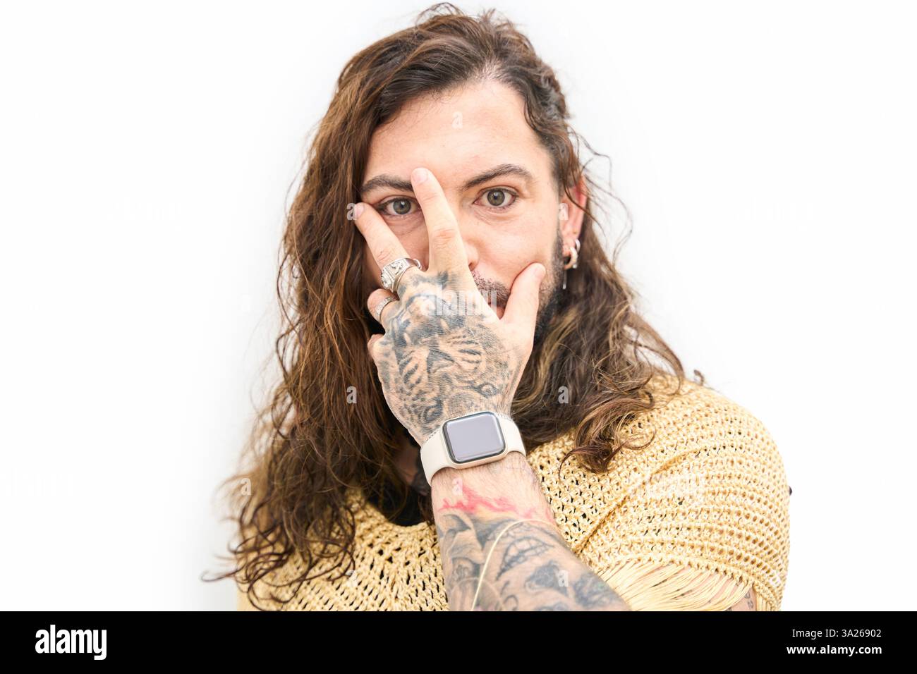 Portrait of a young non binary latin influencer with long hair, beard and tattoos covering face ...