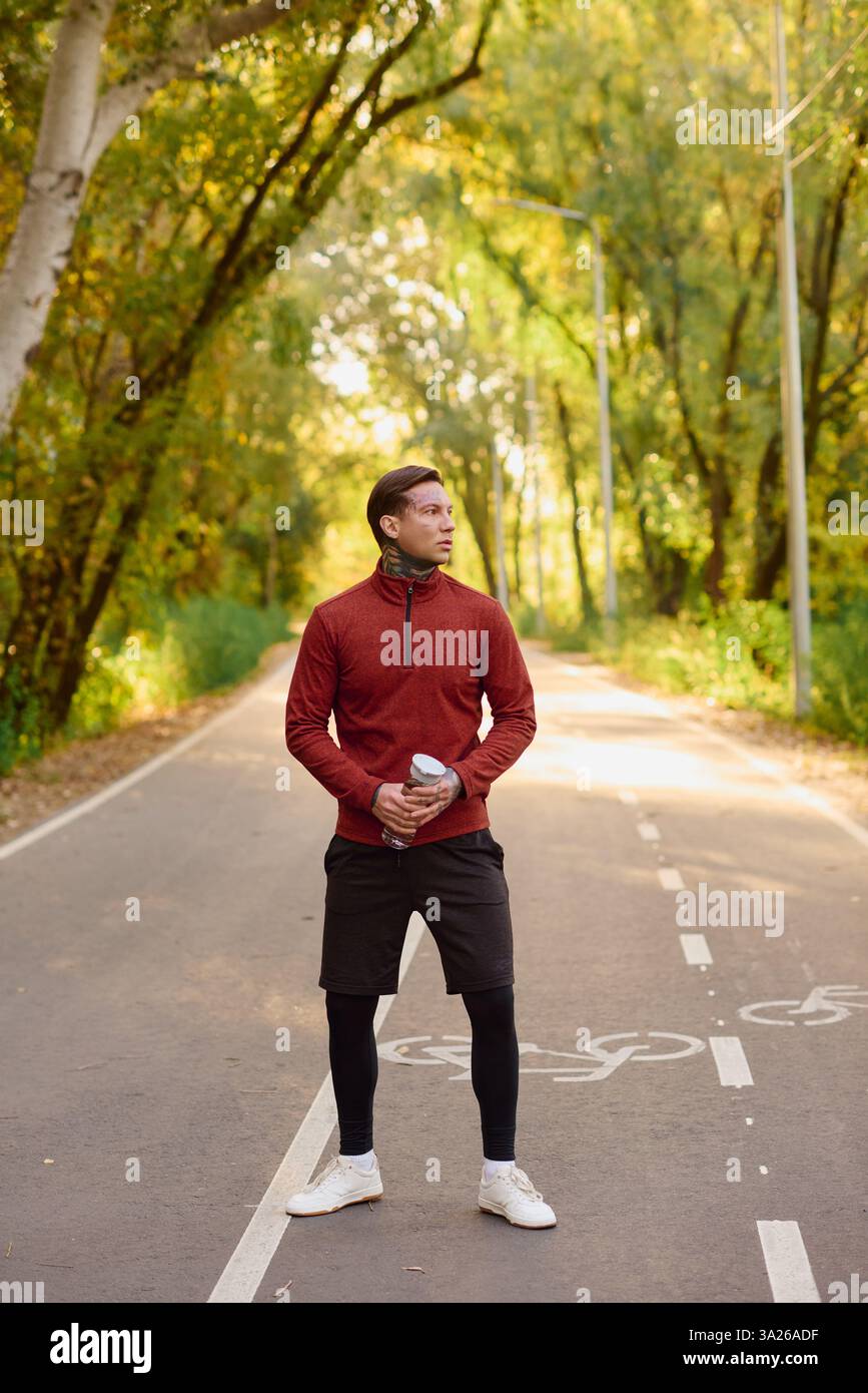 A young man in athletic wear poses confidently on a tree lined path ...