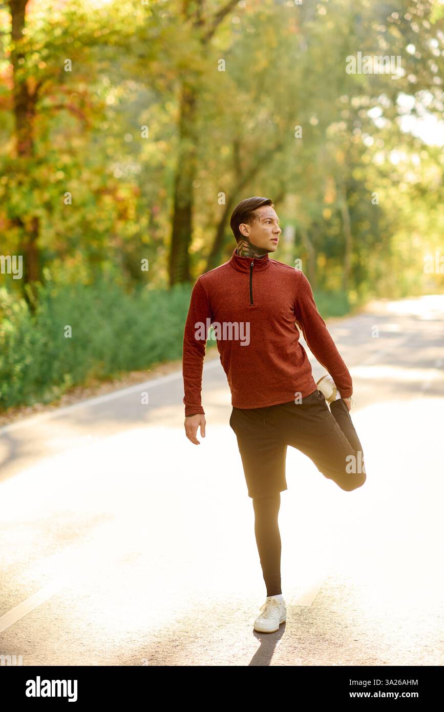 Handsome man with tattoos striking a dynamic pose on a scenic autumn ...