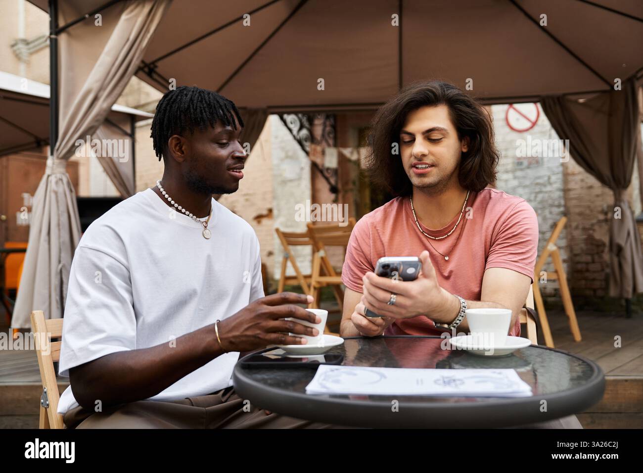 Two handsome men share a joyful moment at a cafe while looking at a ...