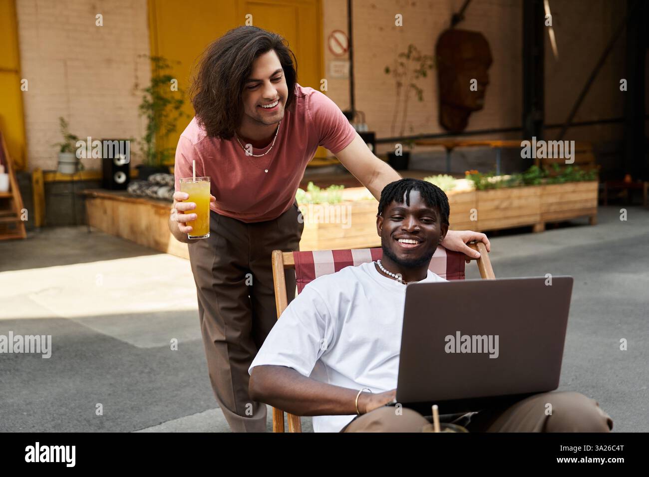 Two handsome men share laughs and drinks at a cafe while working on a ...