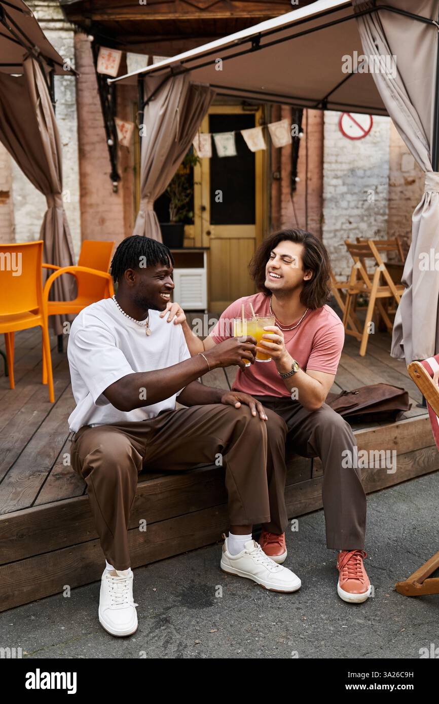 Two handsome men toast with drinks at a cozy outdoor cafe, celebrating ...