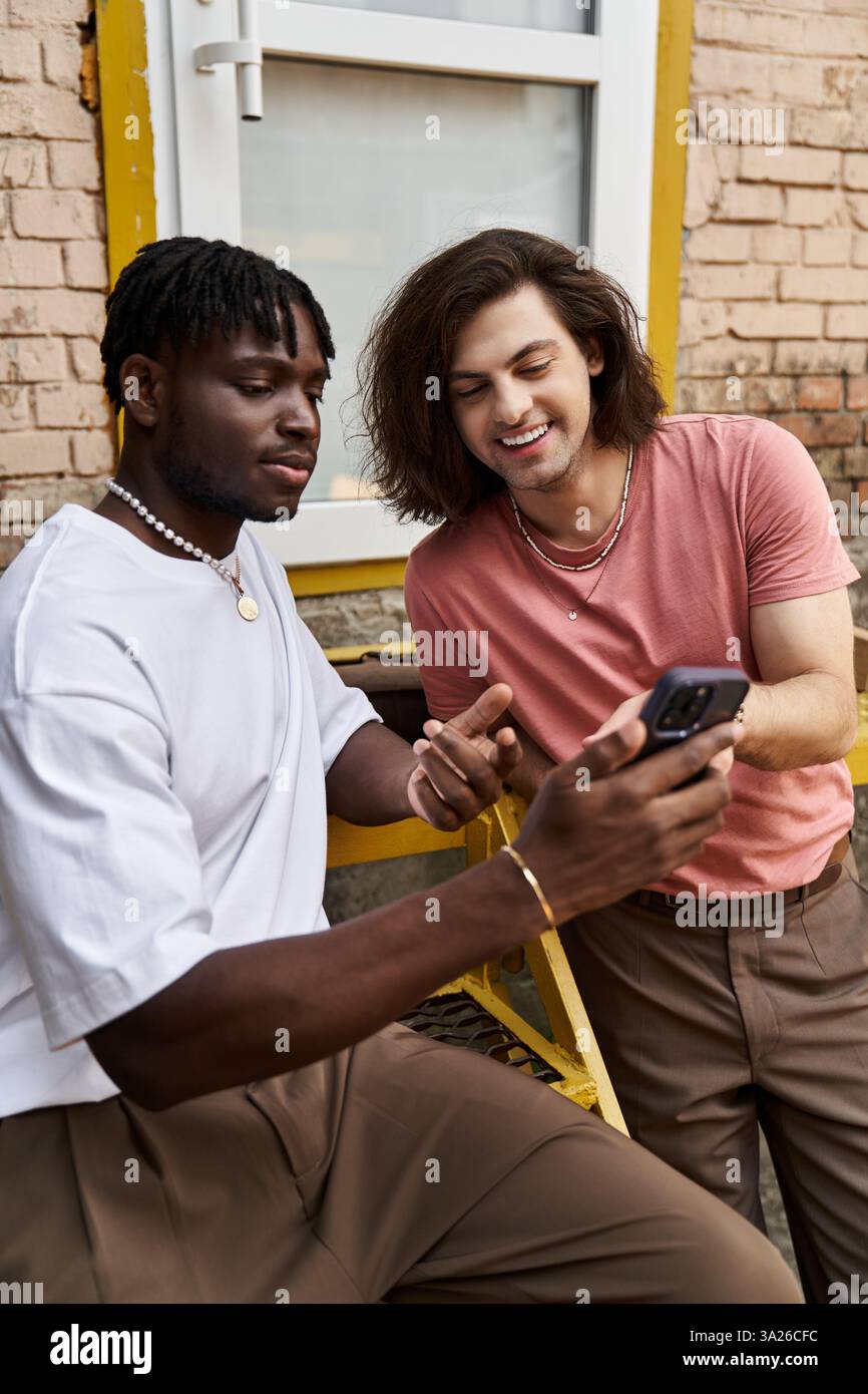 Two handsome men on a date smile and laugh while checking their phones ...