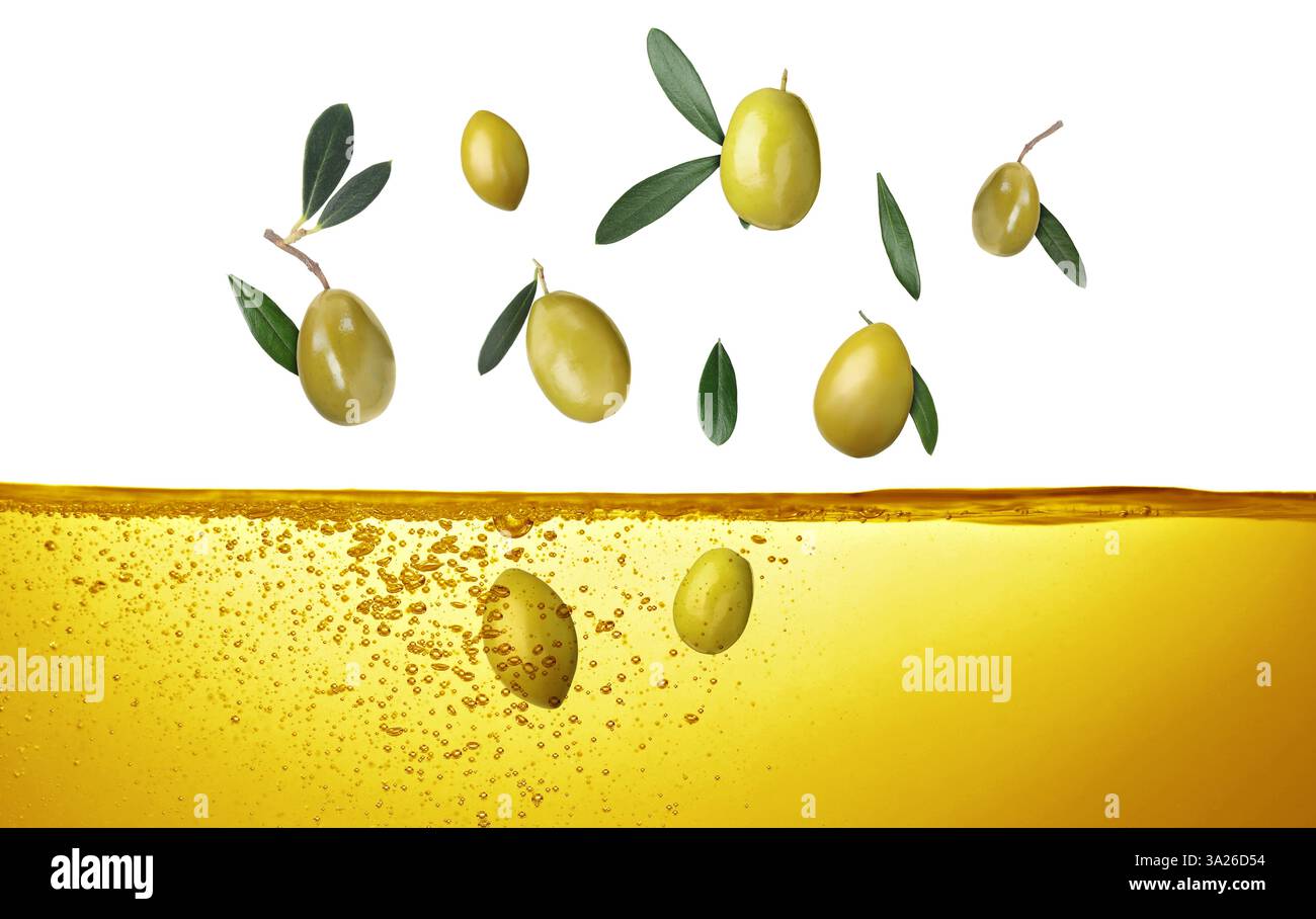 Green olives and leaves falling into cooking oil on white background ...