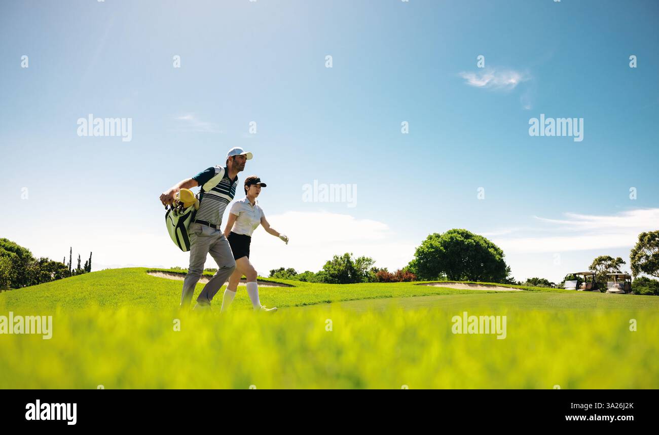 A female golfer and her caddy walk on a golf course under a clear blue ...