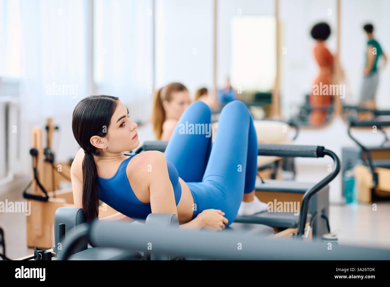 A young woman uses a reformer in a dynamic pilates workout to boost her ...