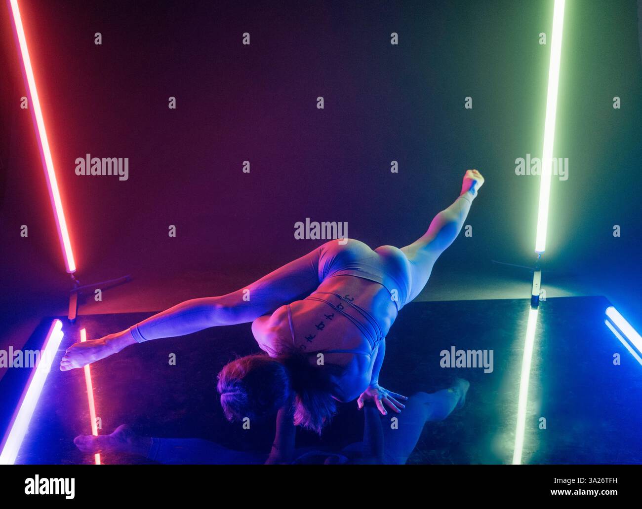 A dancer in a bodysuit performs a graceful pose amid colorful neon ...