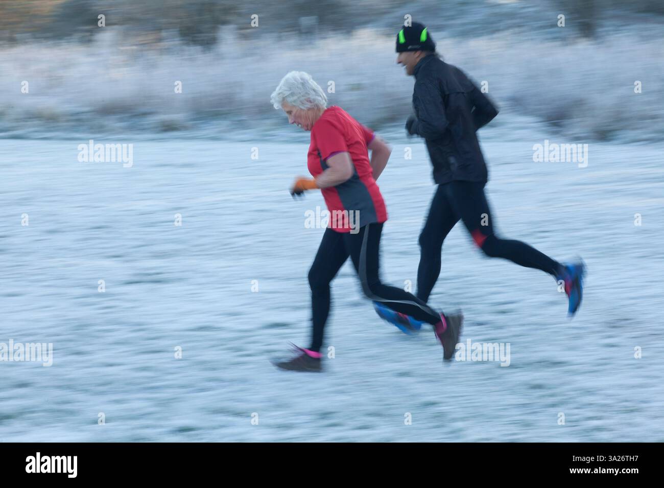 Two people jogging through a snowy field, dressed in winter running ...