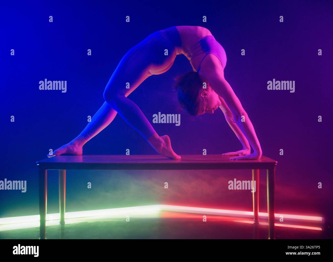 Woman performing a backbend on a table under vibrant blue and purple ...