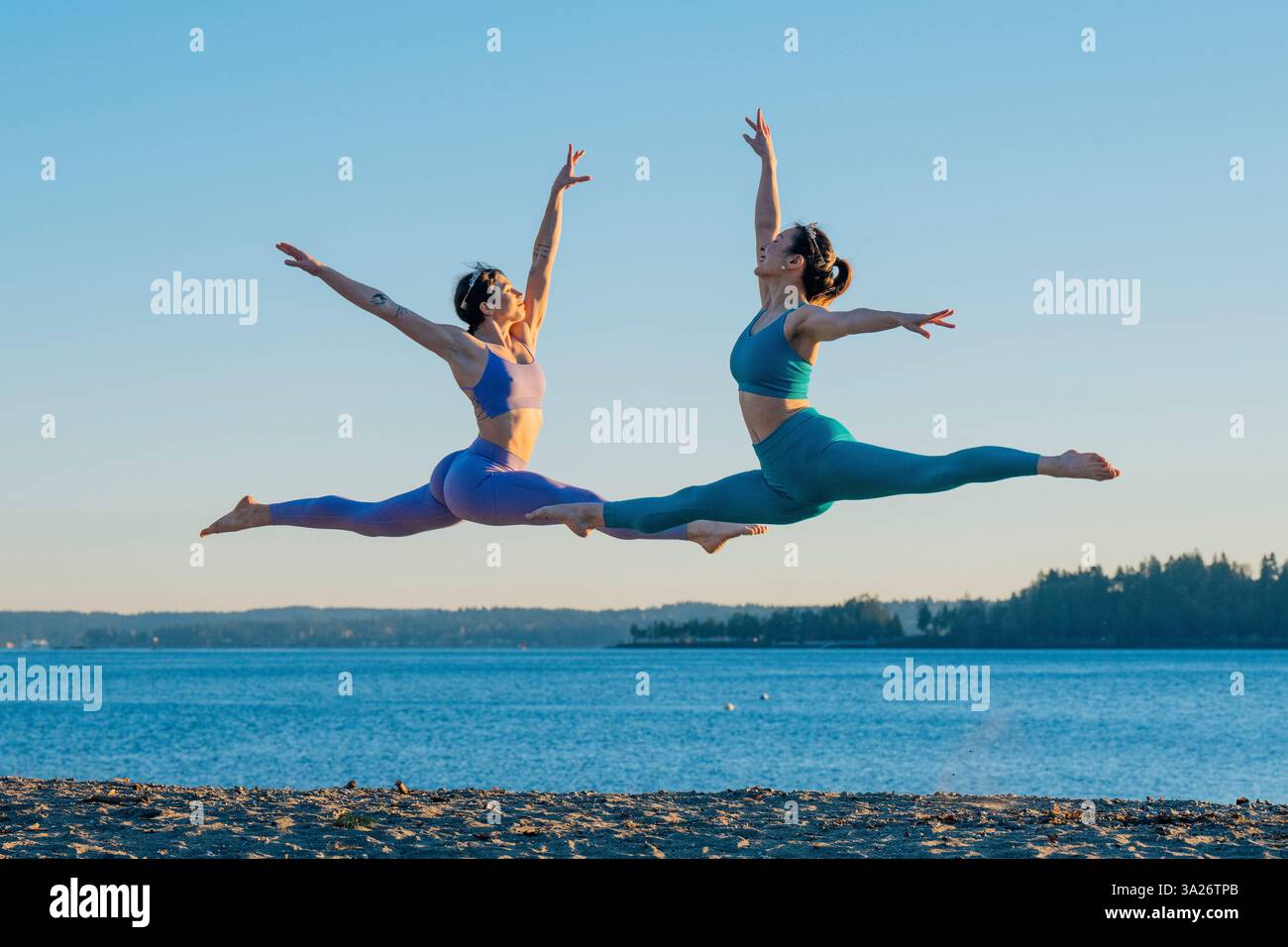Two women performing elegant ballet leaps on a beach with a scenic ...