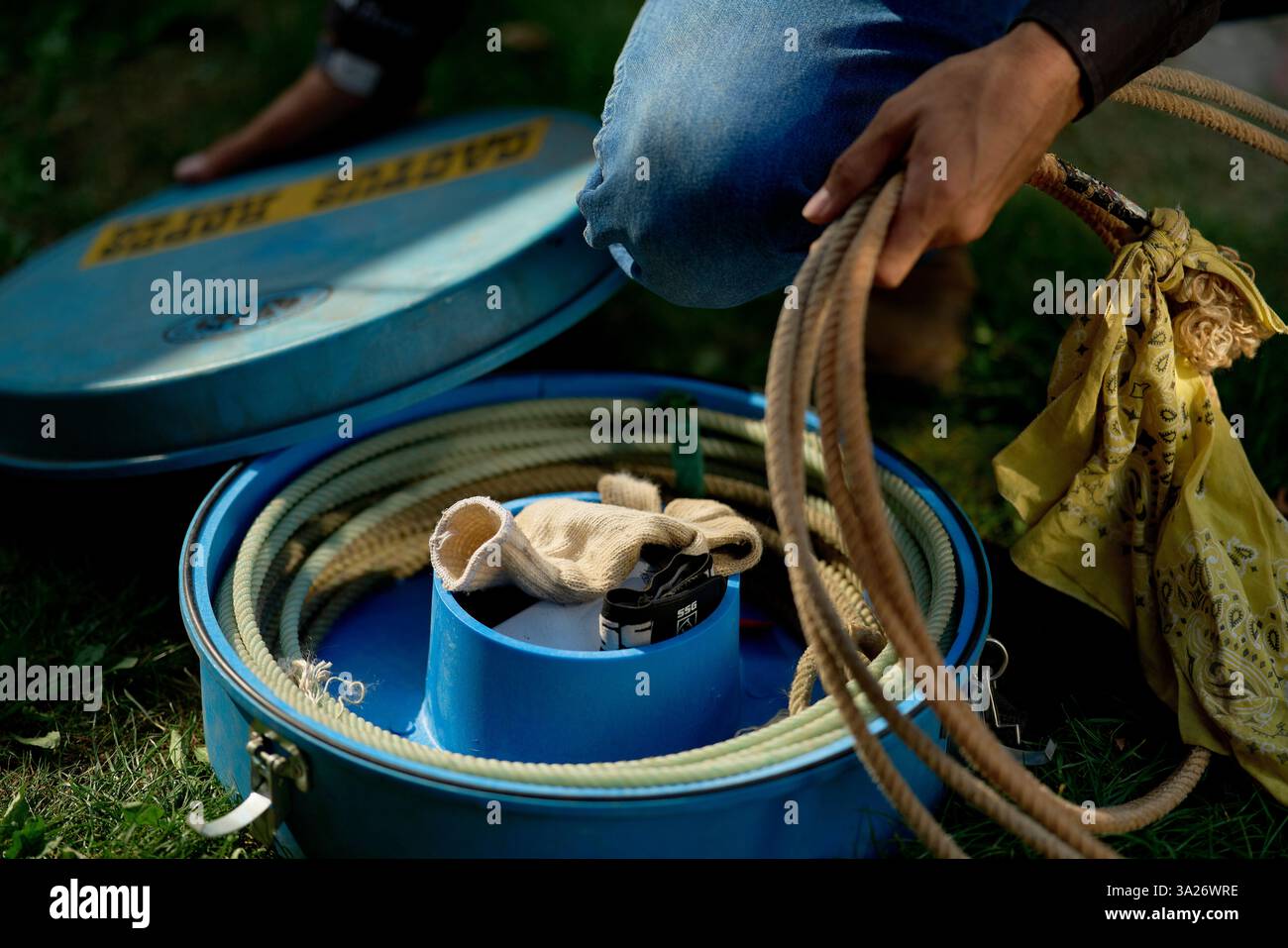 A person handling coiled ropes and tools in a blue container on grass ...