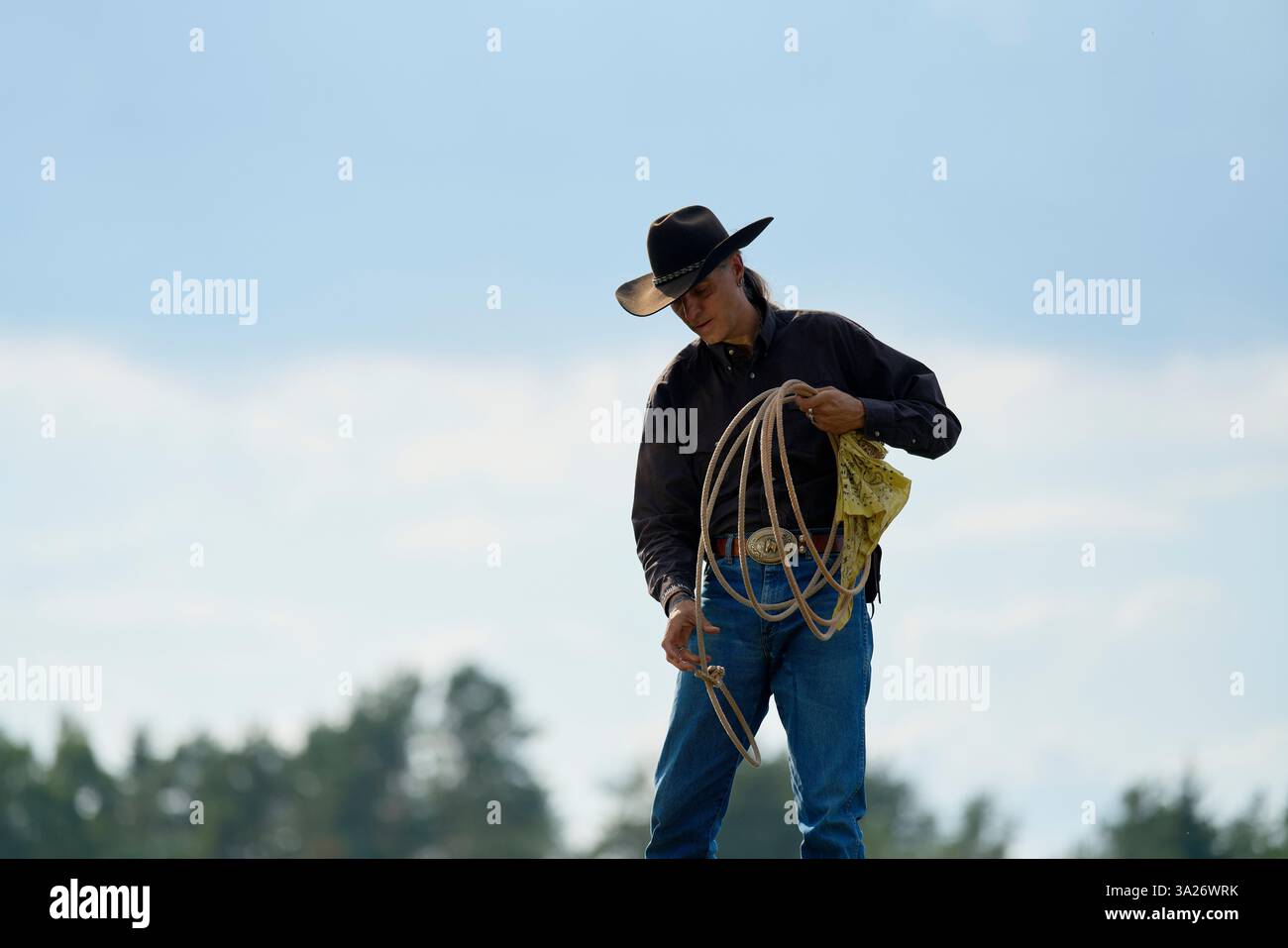 Cowboy holding a lasso and wearing a hat, standing against a clear blue ...
