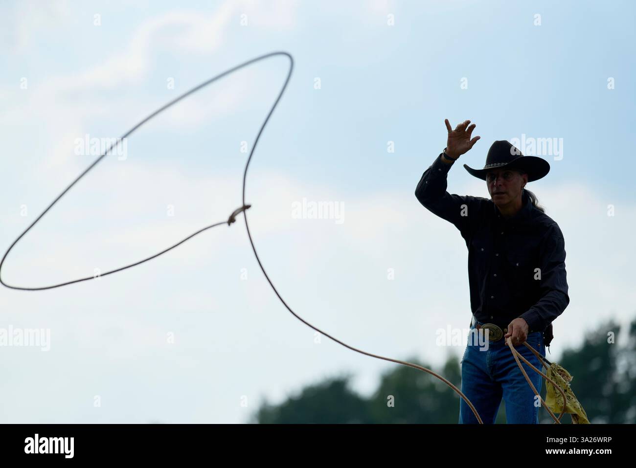 Cowboy skillfully twirling a lasso in an outdoor setting under a clear ...