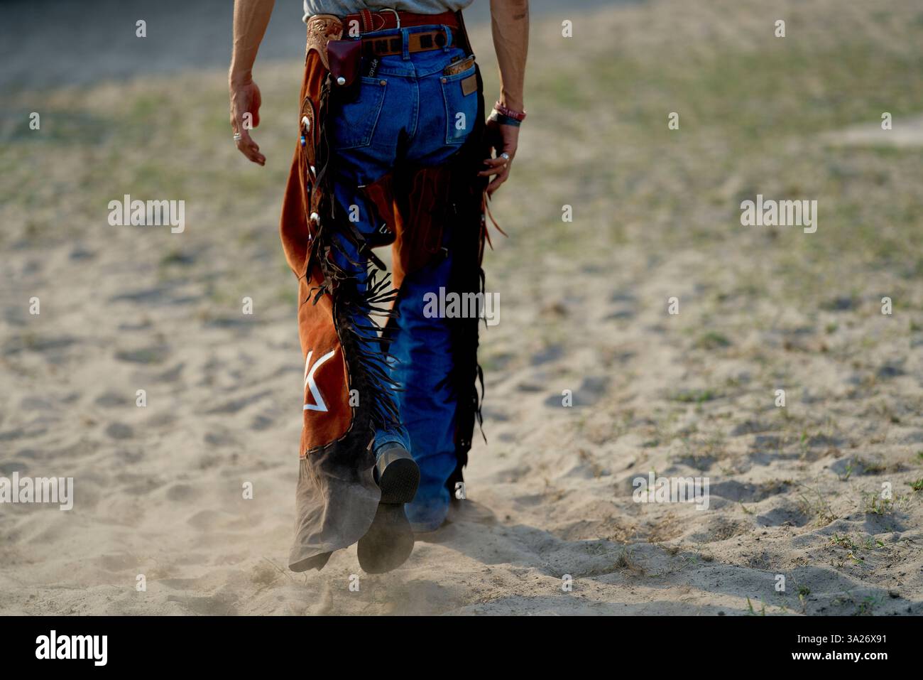 Man in cowboy attire walks on a sandy path, wearing blue jeans and ...