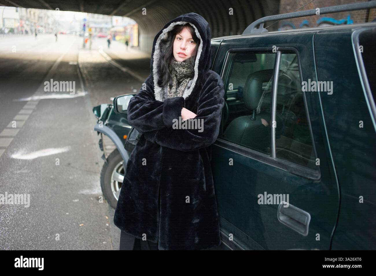 Woman in a fur coat standing by a green car that just had an accident ...