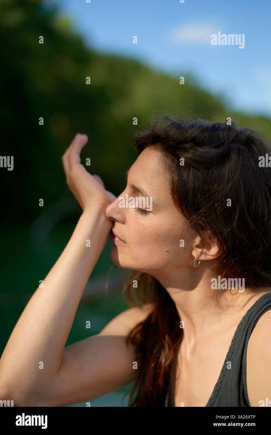 Woman in profile smelling scent on her wrist with closed eyes outdoors ...